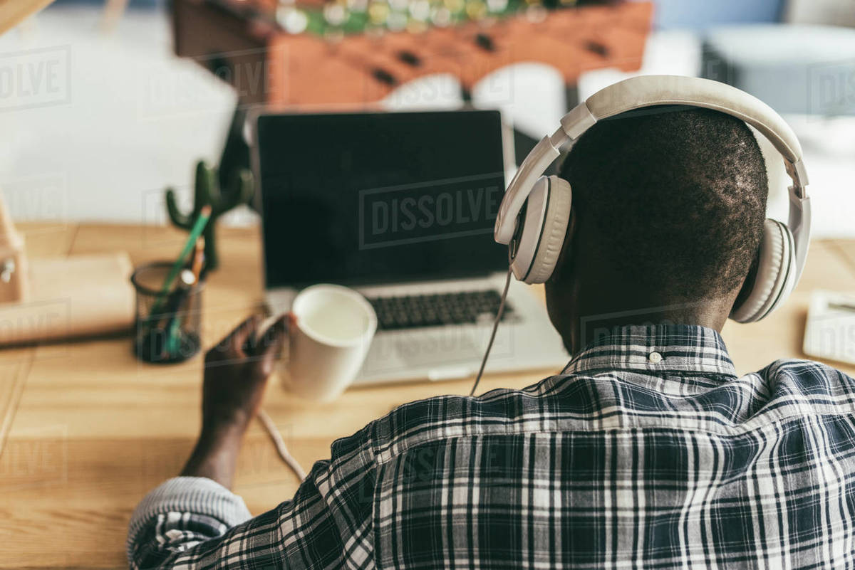 Back view of man in headphones using laptop - Royalty-free Stock Photo ...