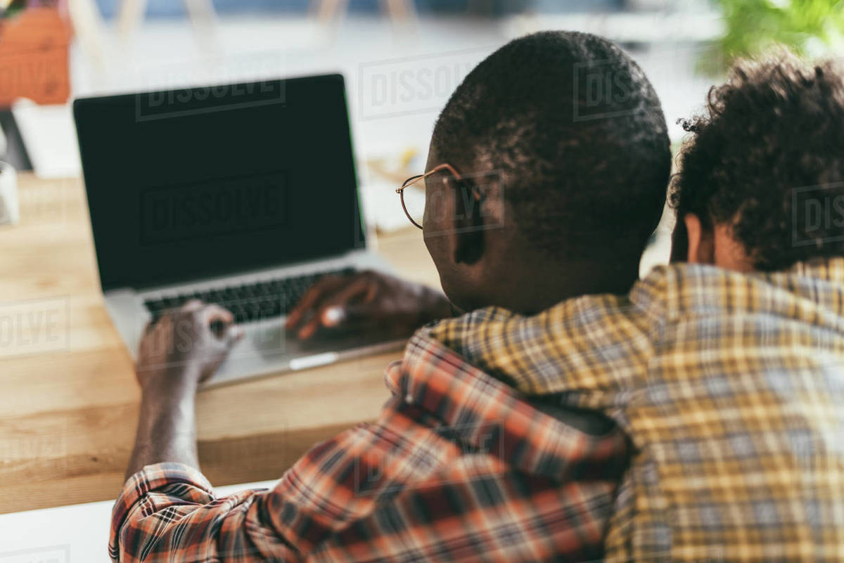 Back view of African American father and son using laptop with blank ...