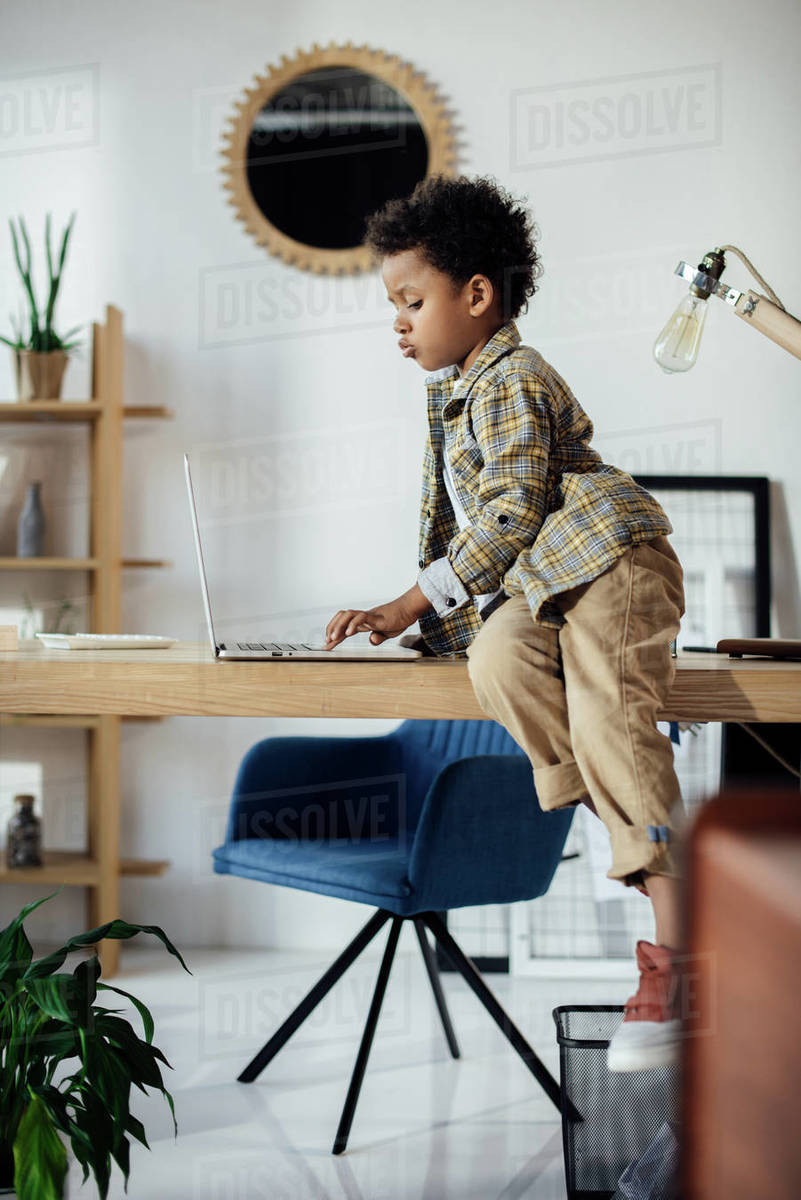 Adorable little boy sitting on table and using laptop - Stock Photo ...