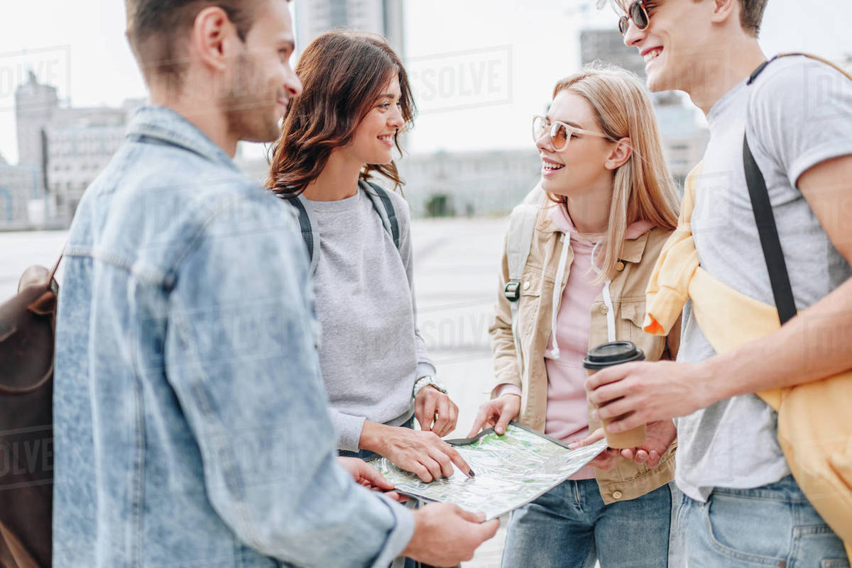 Smiling tourists pointing at map while spending time together in city ...