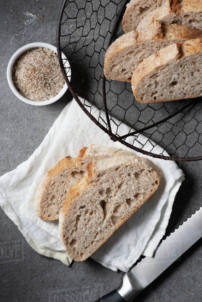 Flat lay with cut loaf of bread, knife and white linen on grey tabletop ...
