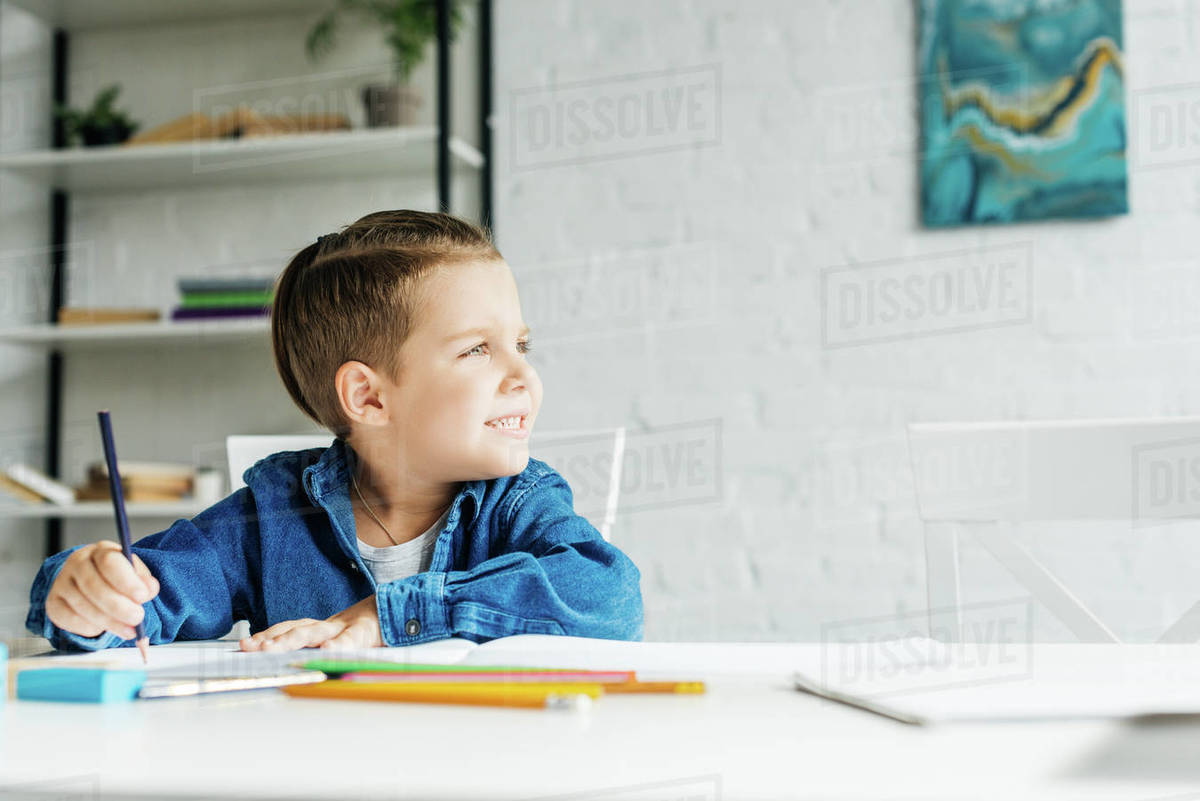 Cute little kid drawing with color pencils at home and looking away ...