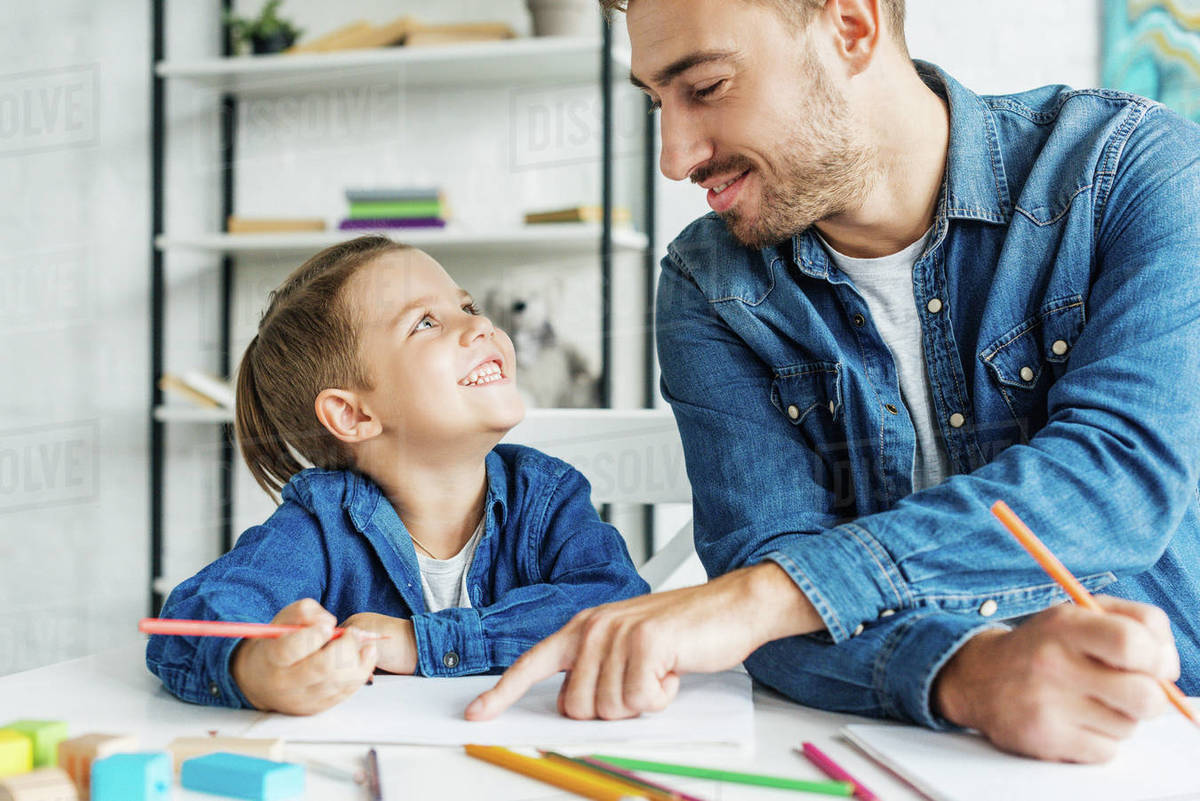 Smiling young father drawing with son at home - Stock Photo - Dissolve