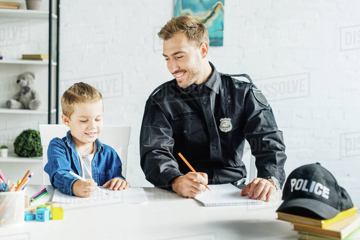 Smiling young father in police uniform and son drawing together at home ...