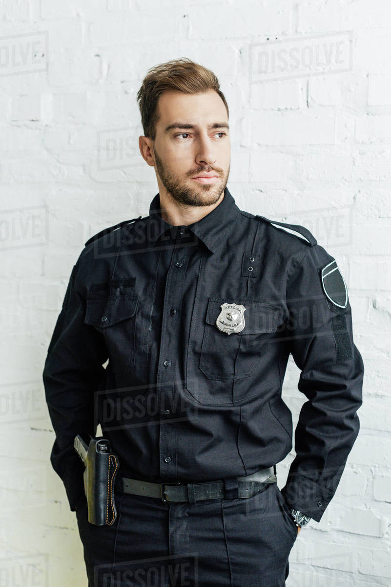 Portrait of handsome young policeman in front of white brick wall ...