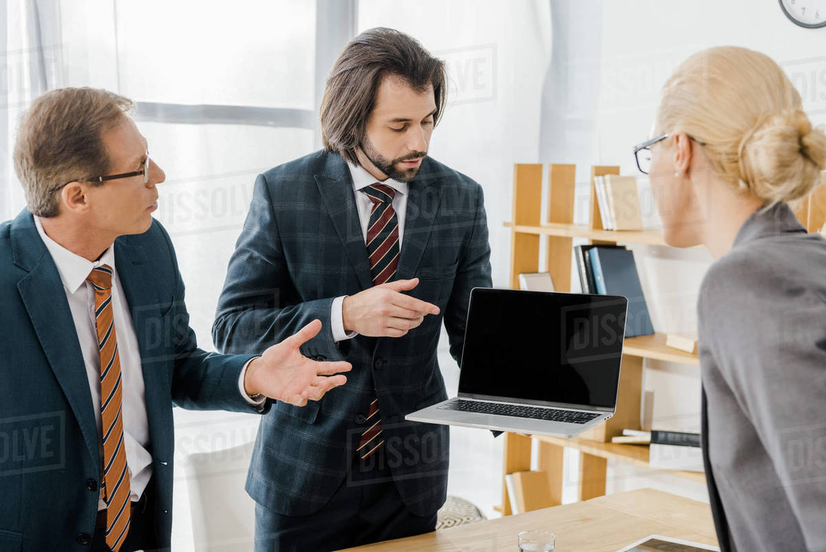 Young male insurance agent standing with workers and pointing at laptop ...