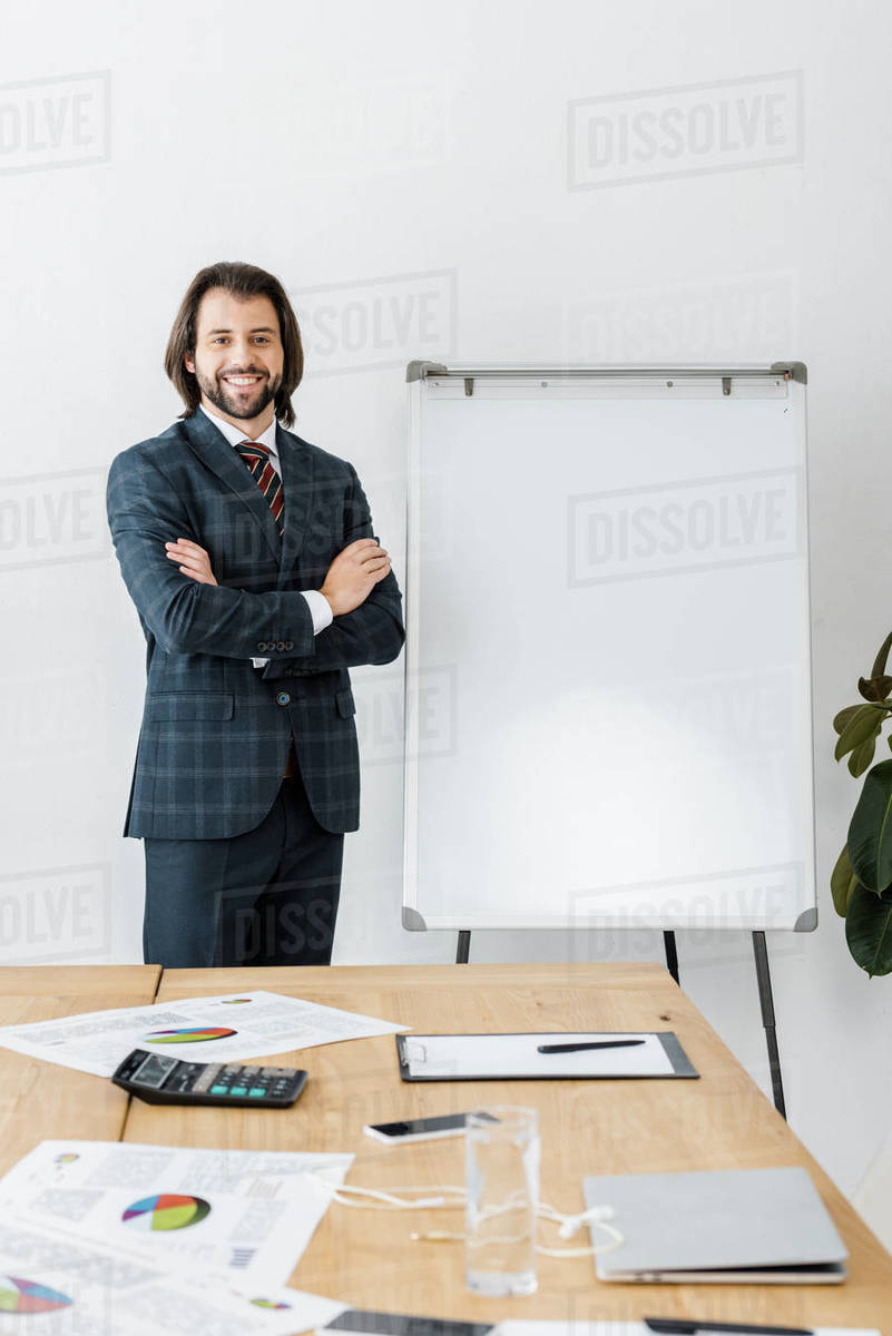 Young smiling male insurance agent standing with arms crossed near ...
