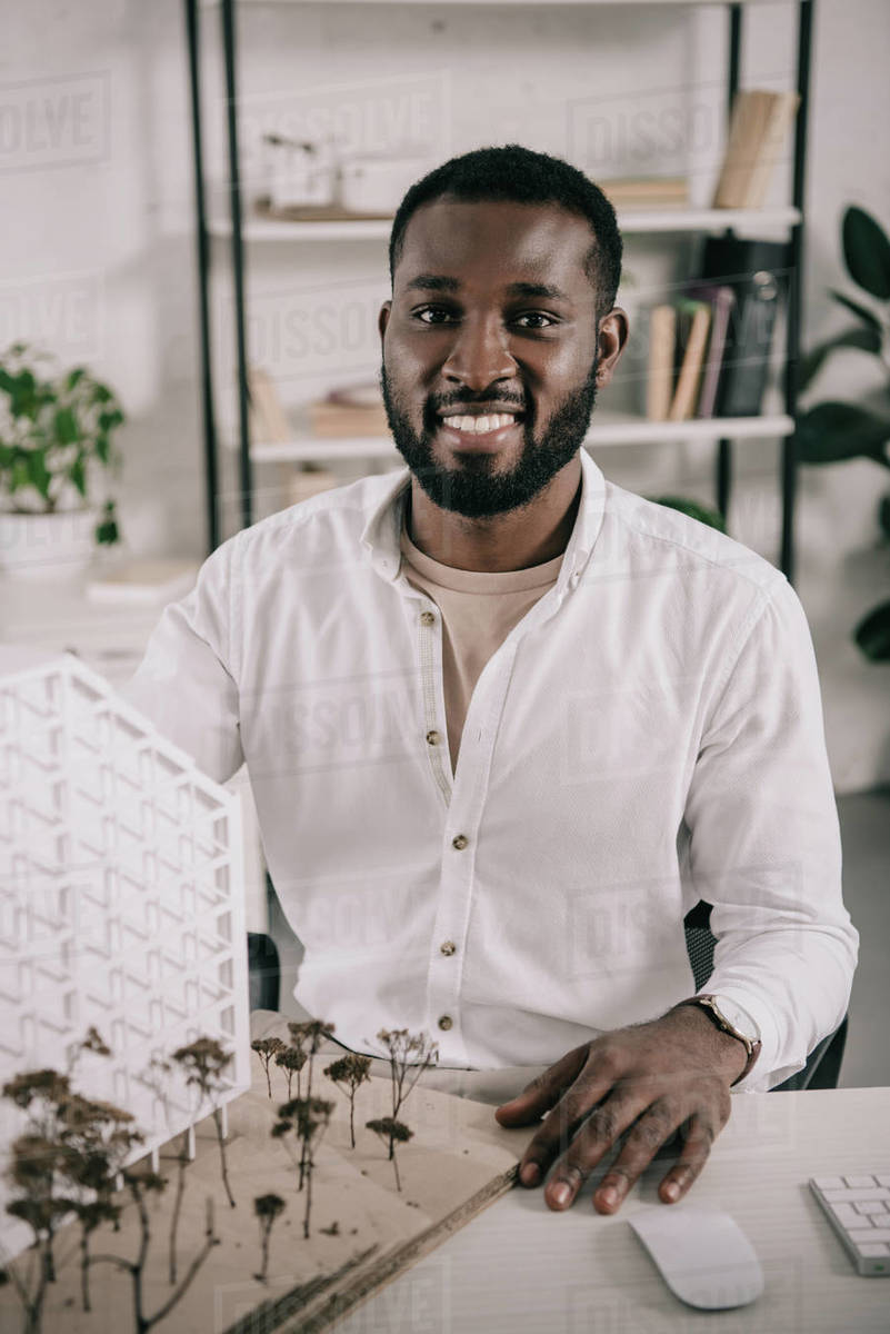 Smiling African American architect sitting near architecture model on ...