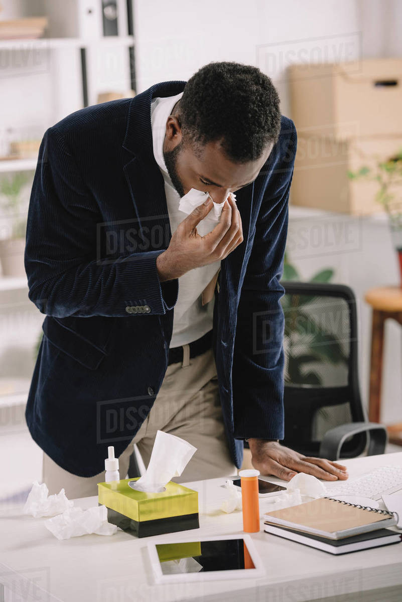 Diseased businessman having cold while working with digital devices in ...