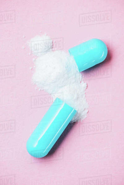 Close-up shot of broken medical capsule with spilled powder on pink ...