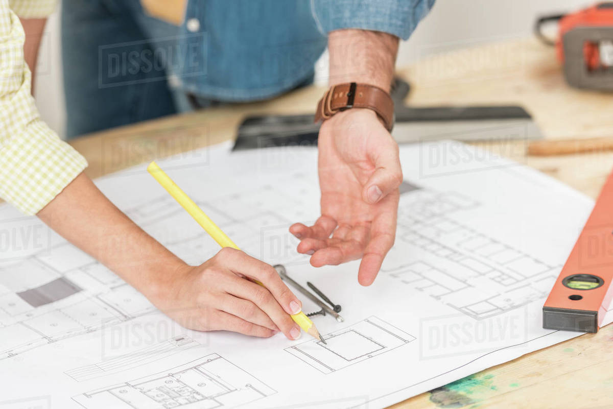 Close-up partial view of young couple pointing at marking blueprint ...