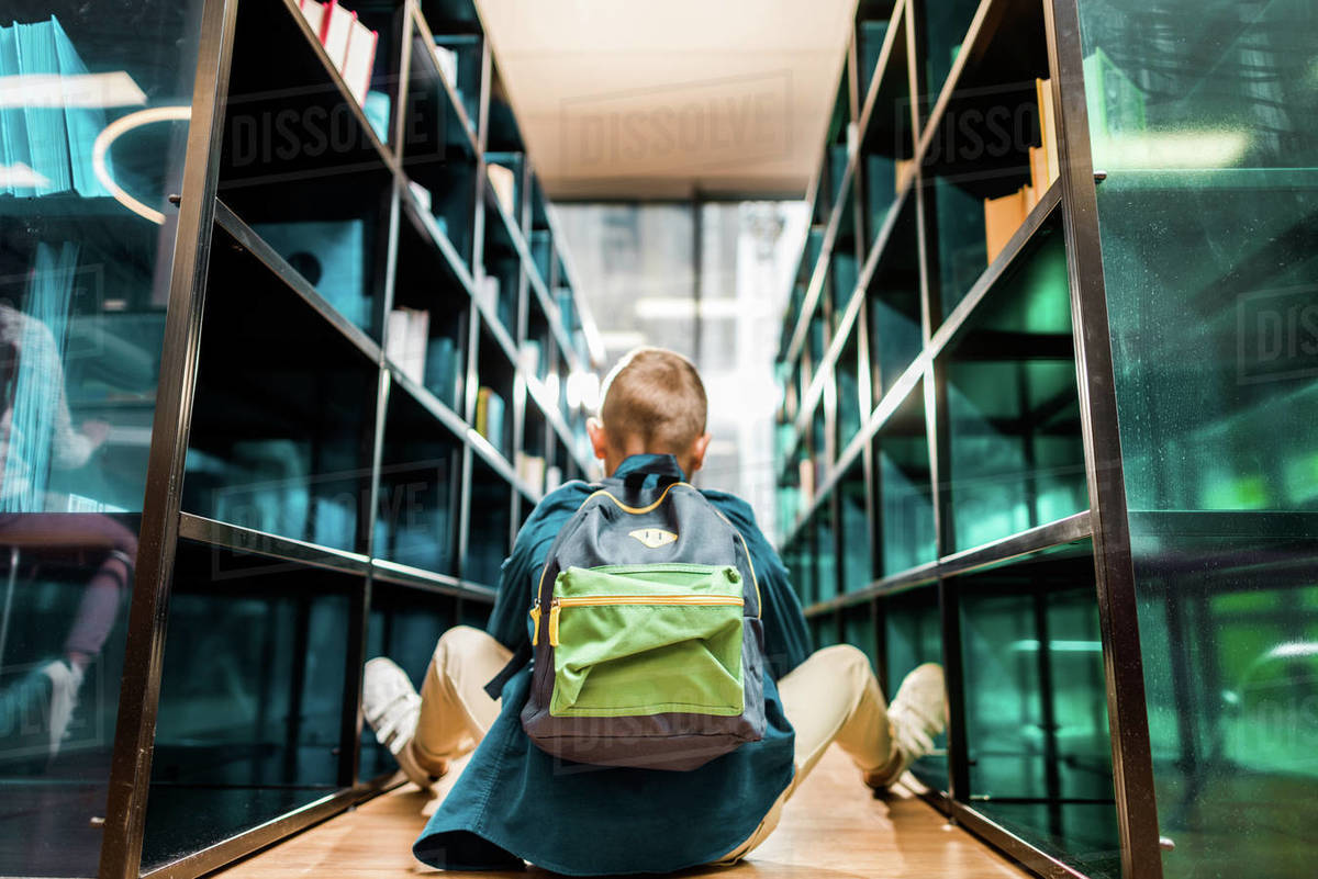 Back view of boy with backpack sitting on floor in library - Royalty ...