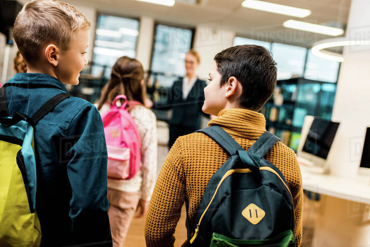 Back view of boys with backpacks looking at each other while visiting ...