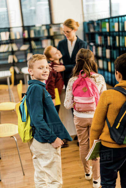 Back view of schoolchildren with backpacks standing with librarian in ...