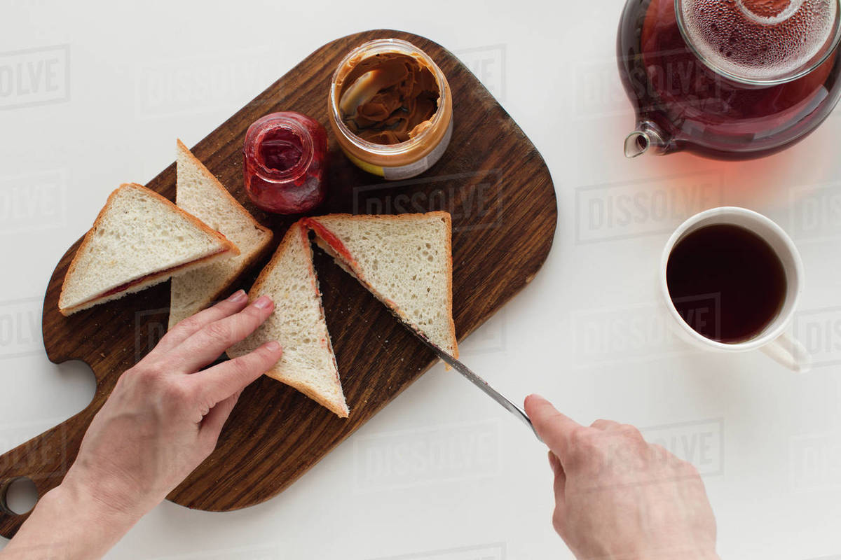 Cropped view of person cutting toasts with jam and peanut butter for ...