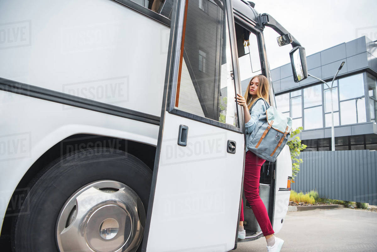 Beautiful young woman with backpack walking into travel bus at street ...