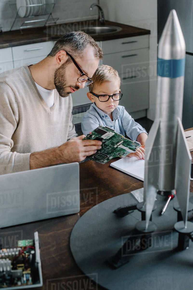 Father and son repairing microcircuit together, rocket model on table ...
