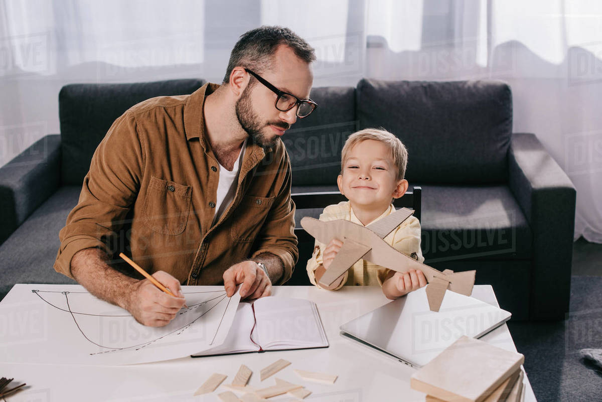 Father in eyeglasses and cute little son modeling plane together at ...