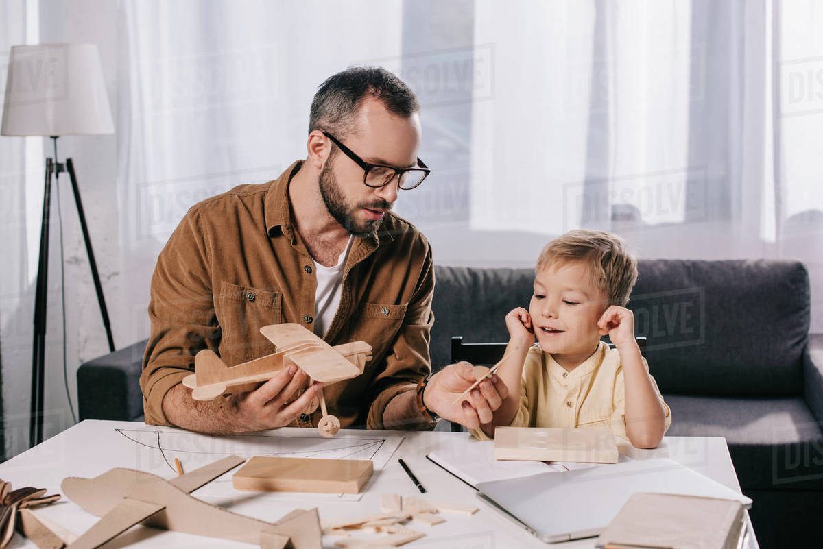 Father in eyeglasses and smiling son modeling plane together at home ...