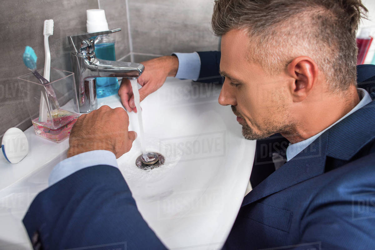 Side view of adult businessman in suit sitting in front of sink in ...