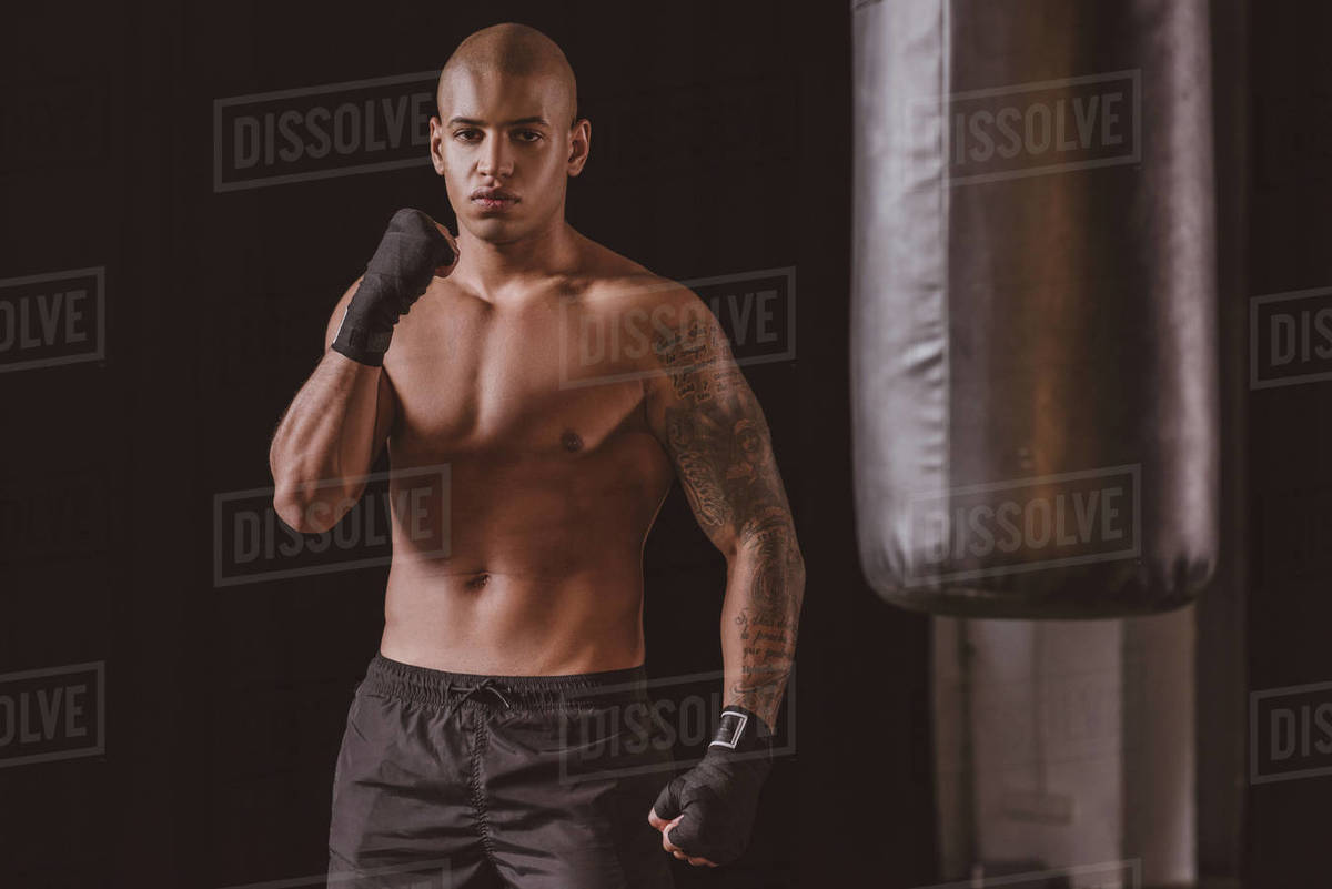Confident African American boxer posing near punching bag at gym ...