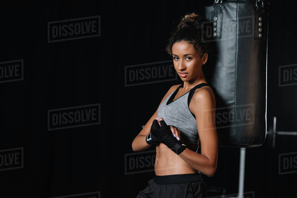 African American female boxer in boxing bandage posing near punching ...