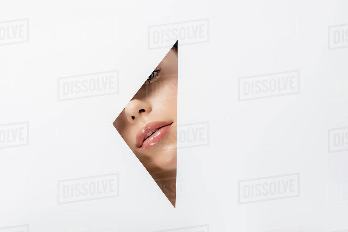 attractive young woman looking at camera through hole on white - Stock ...