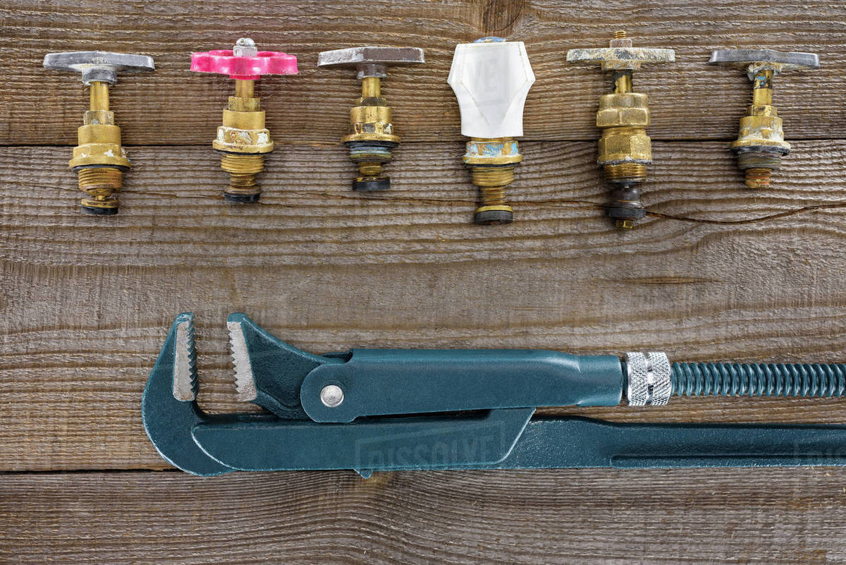 top view of pipe wrench and various plumbing valves on rustic wooden ...