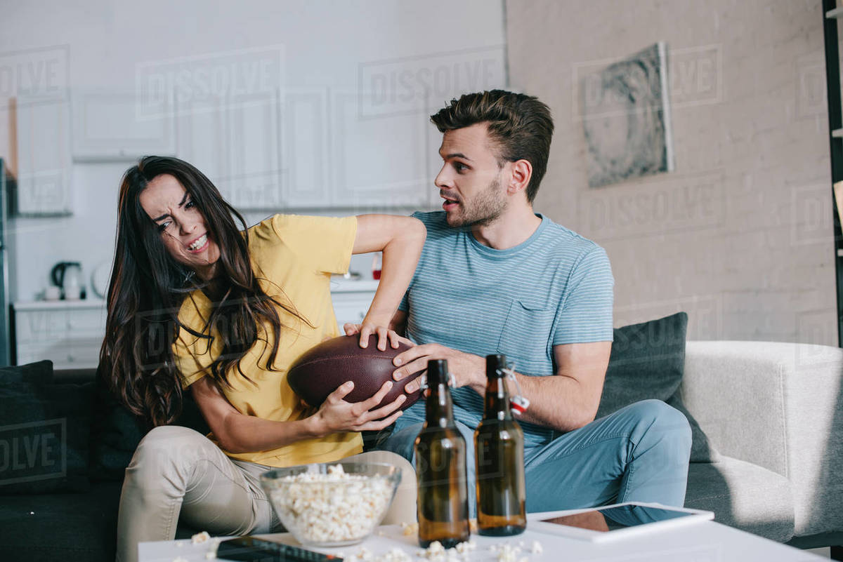 Angry young woman fighting for American football ball with husband ...