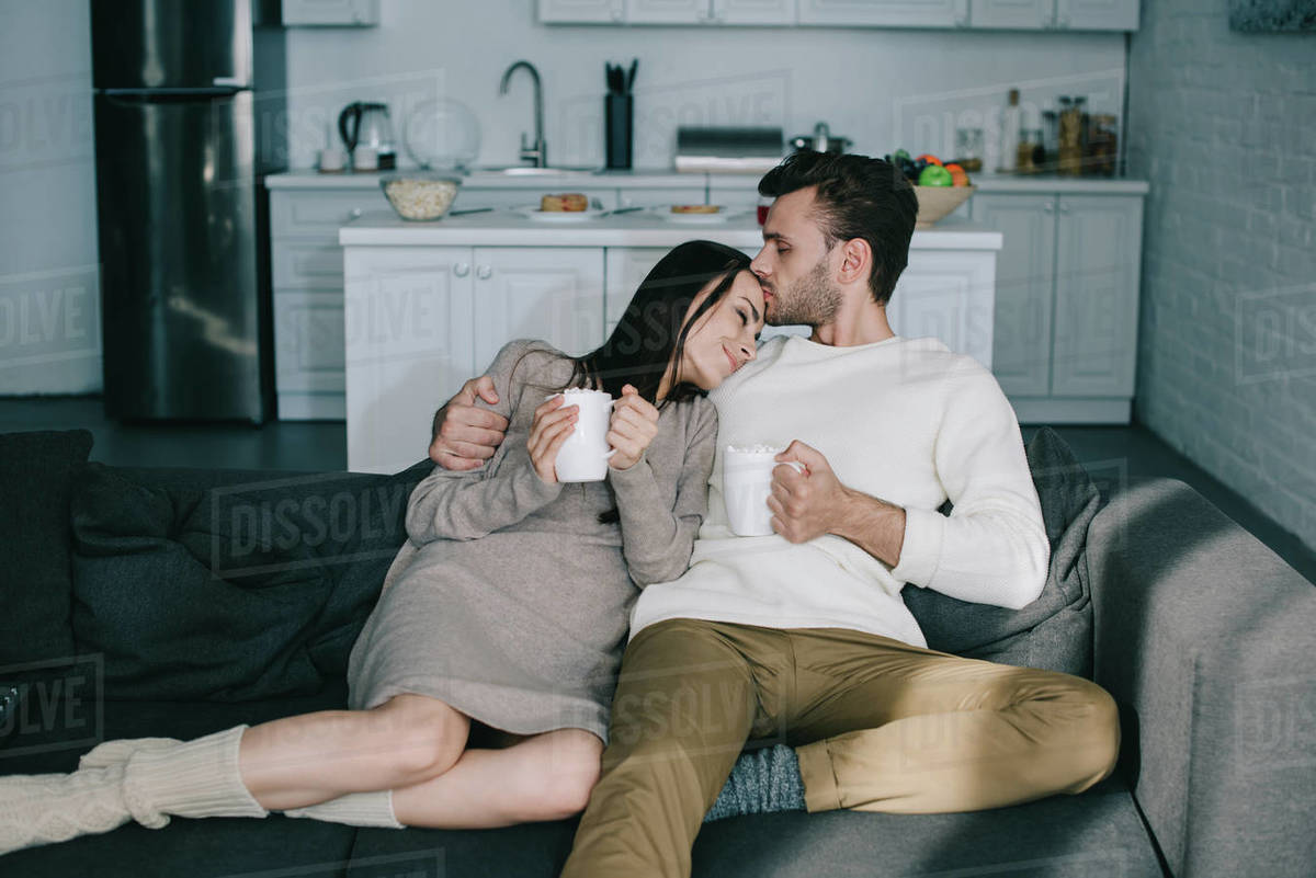 Beautiful young couple with cups of cocoa with marshmallow cuddling on ...