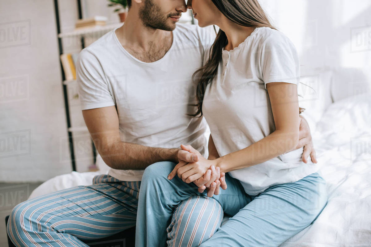Cropped shot of young couple cuddling while sitting on bed in morning ...