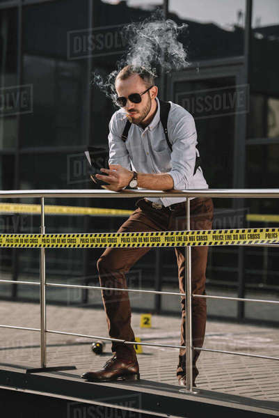 Male detective smoking and looking at notes leaning on the fence ...