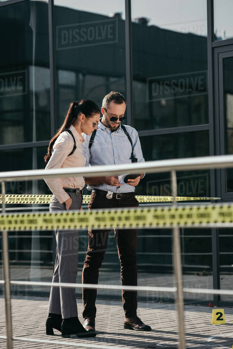 Male and female detectives standing at crime scene and looking at ...