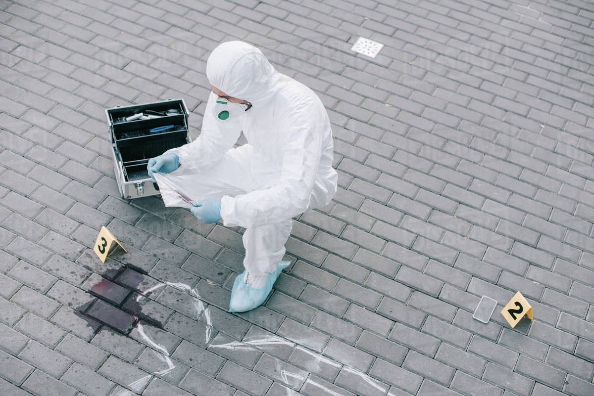 Male Criminologist In Protective Suit And Latex Gloves Explore Evidence