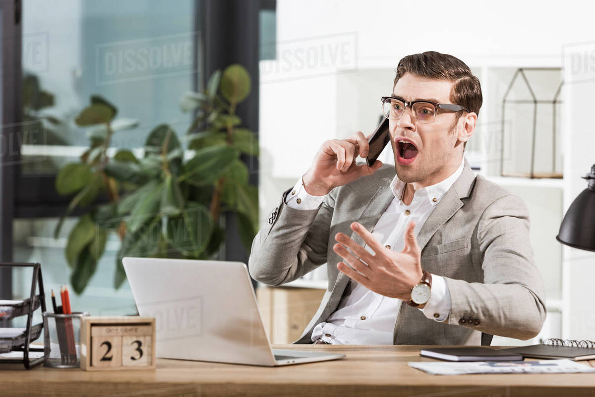 angry businessman talking by phone and screaming at workplace in office ...