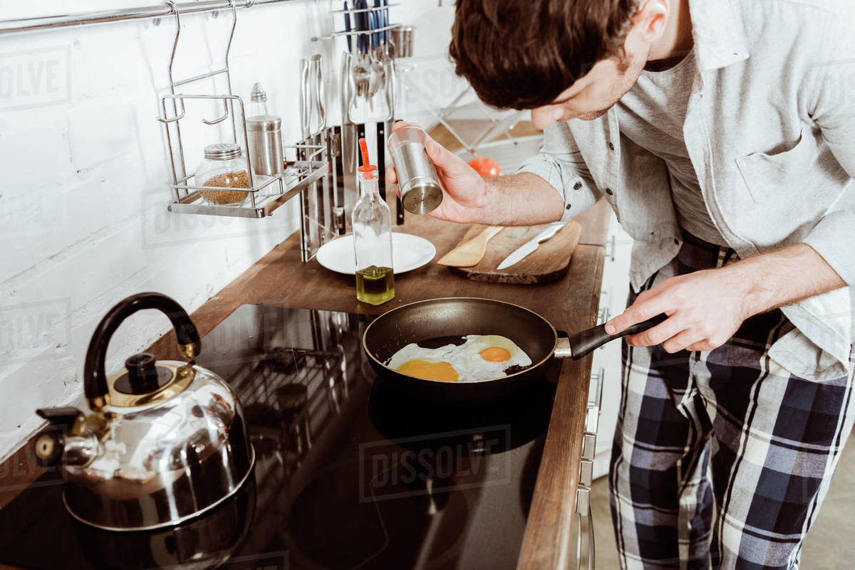 partial view of young man cooking scrambled eggs on frying pan in ...