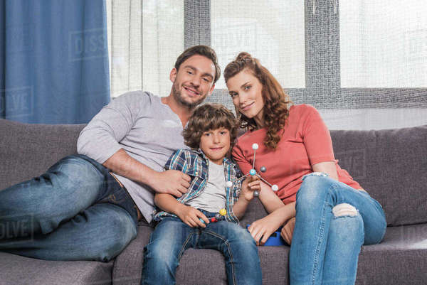 Smiling parents and little boy with atoms model looking at camera while ...