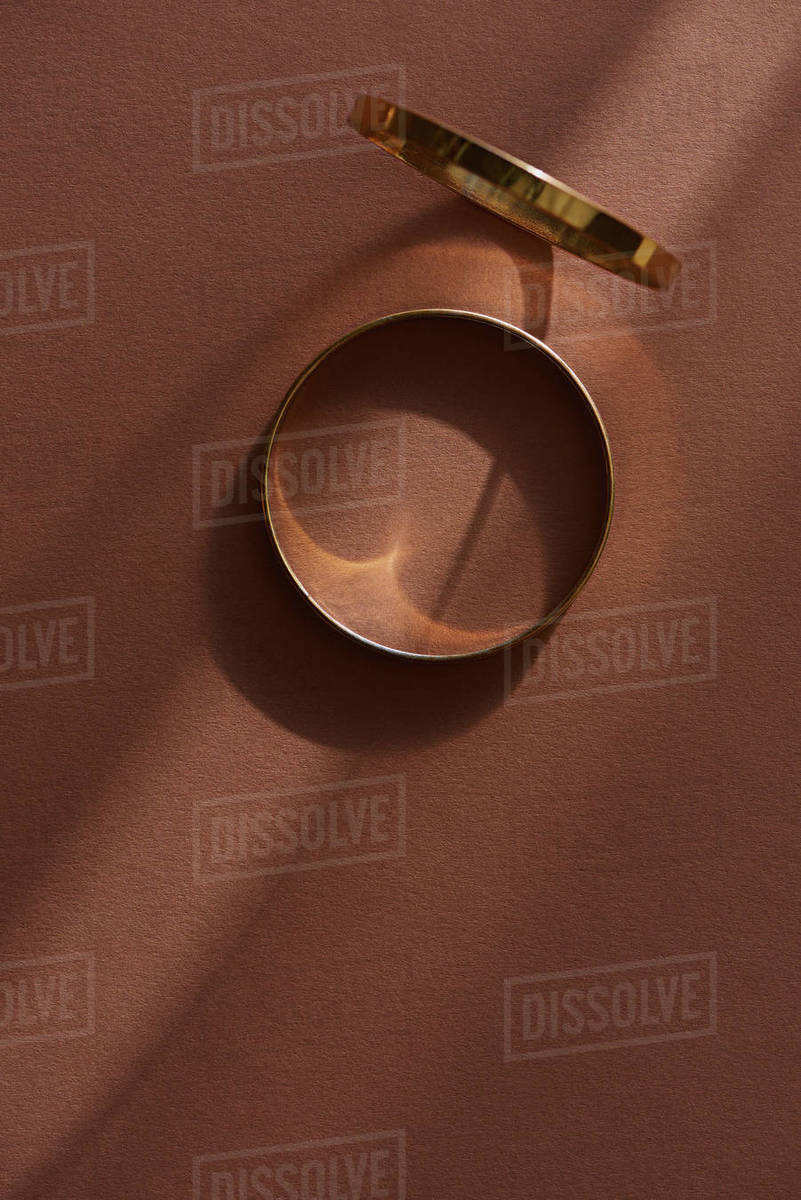 Top view of two beautiful golden rings on brown surface with sunlight ...