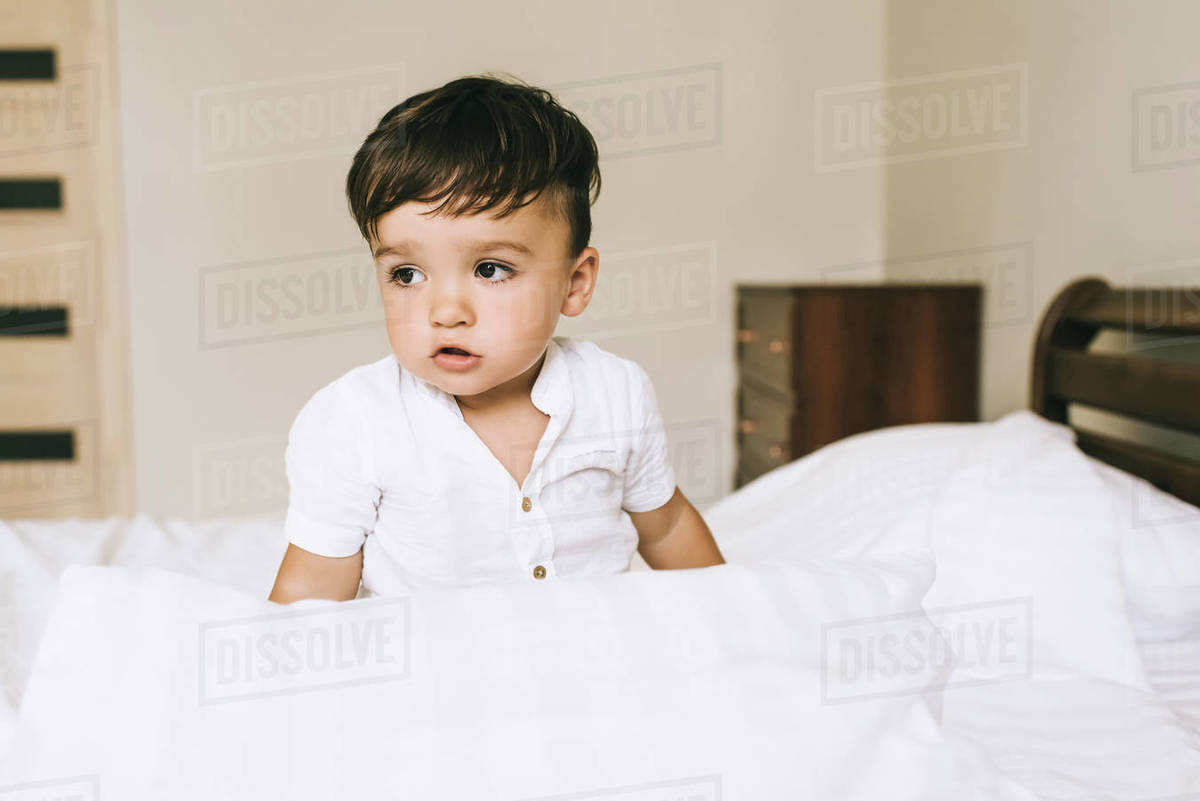 Close-up portrait of adorable little child sitting on bed - Stock Photo ...