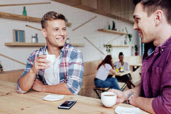 Handsome young men drinking coffee and talking in cafe - Royalty-free ...
