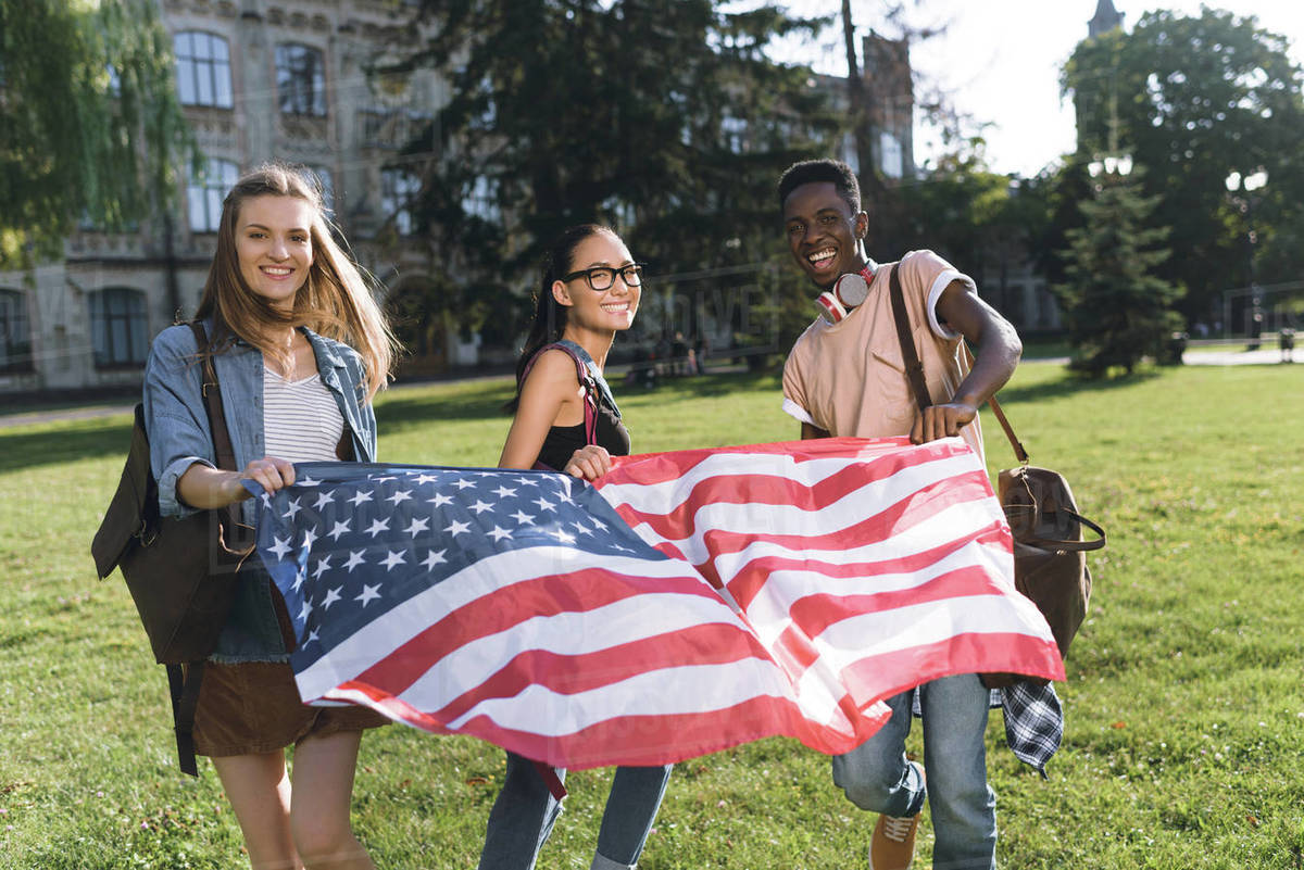Multicultural group of friends holding american flag in park - Royalty ...