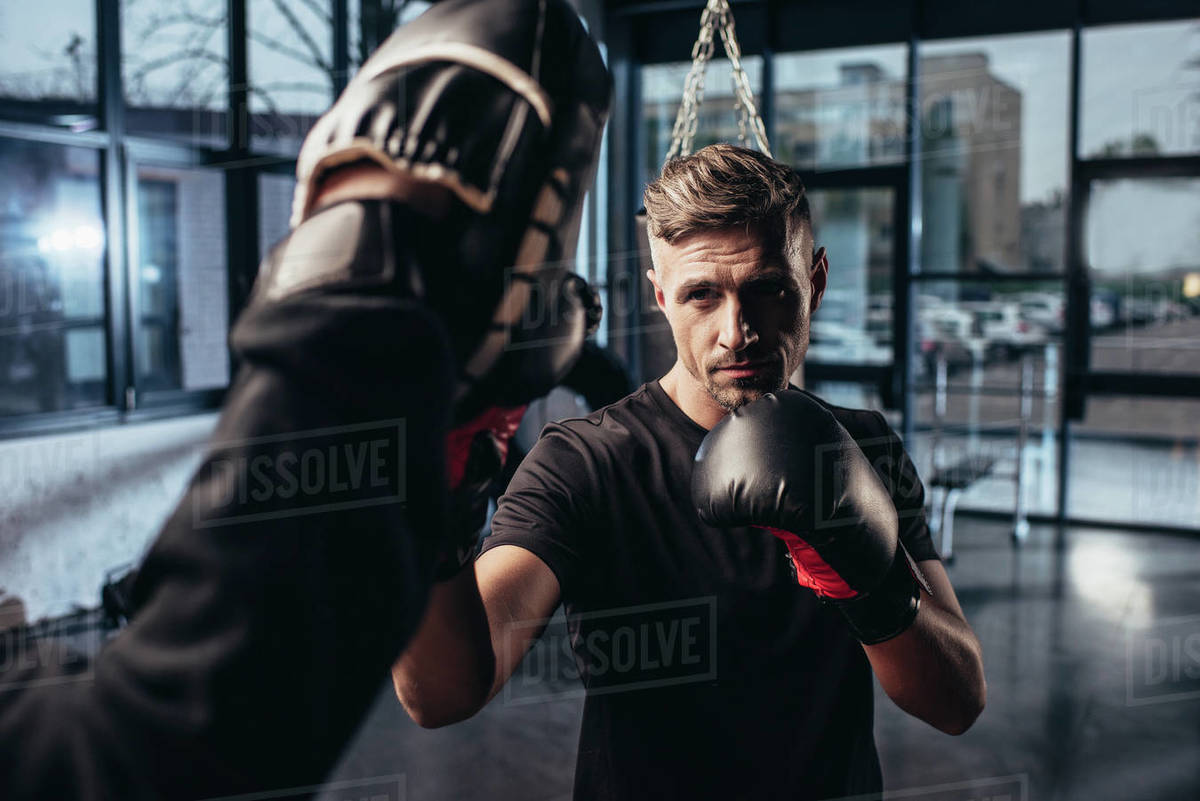 Selective focus of handsome boxer exercising with trainer in gym ...