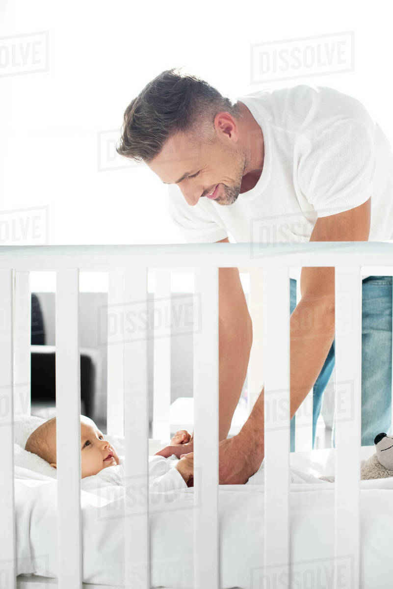 Cheerful father putting infant daughter into baby crib - Royalty-free ...