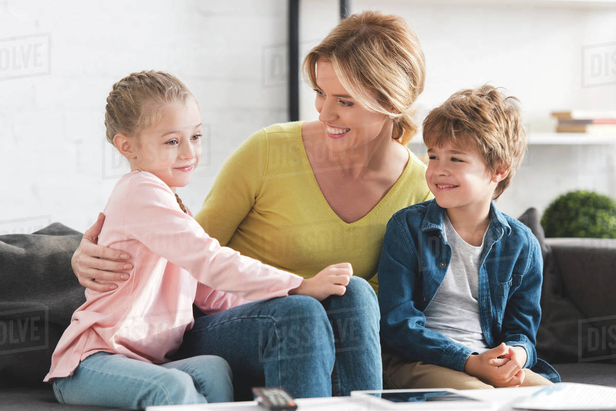 Happy mother looking at adorable smiling children sitting together on ...