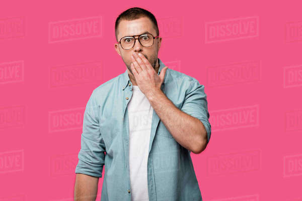 shocked young man holding hand over mouth and looking at camera ...