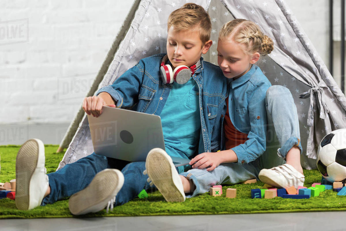adorable little brother and sister using laptop near tent at home ...