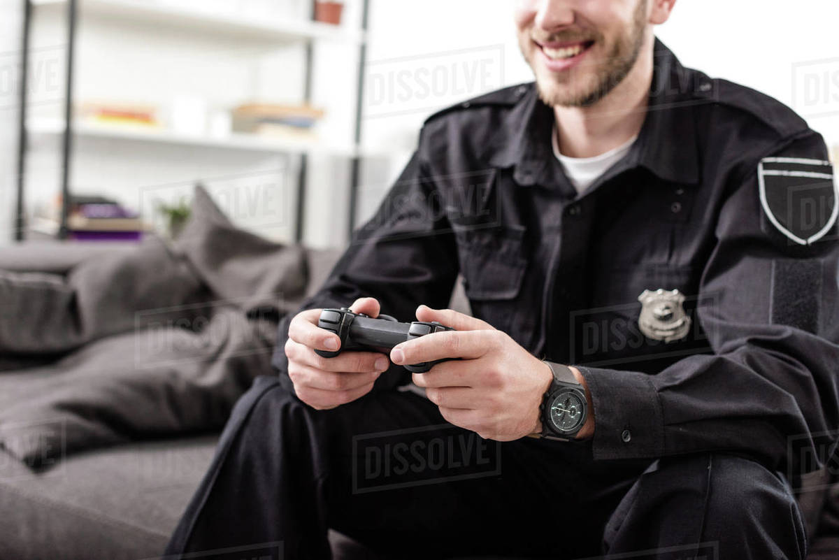 cropped view of policeman with gamepad sitting on couch and playing ...