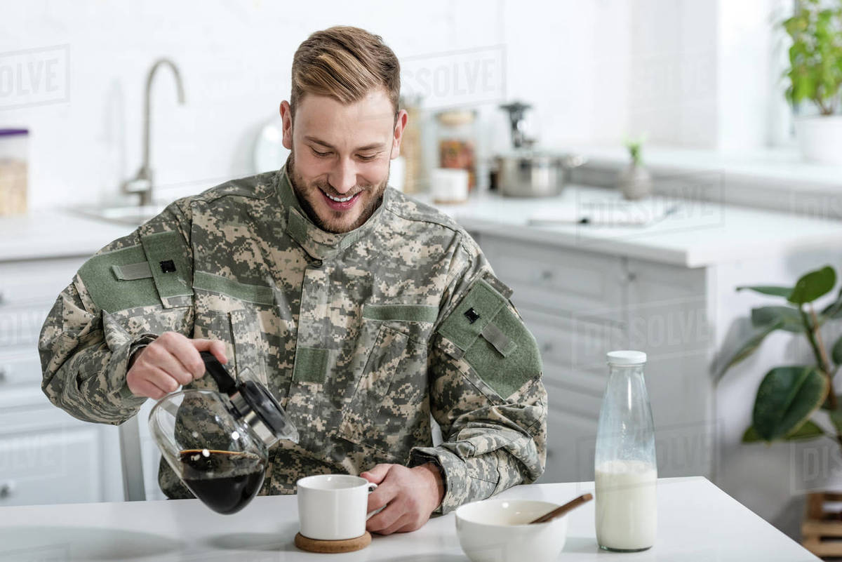 Handsome soldier in uniform smiling and pouring coffee in cup at ...