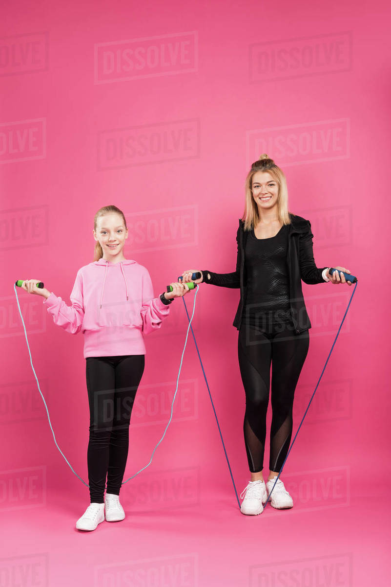 sportive mother and daughter in sportswear posing with skipping ropes ...