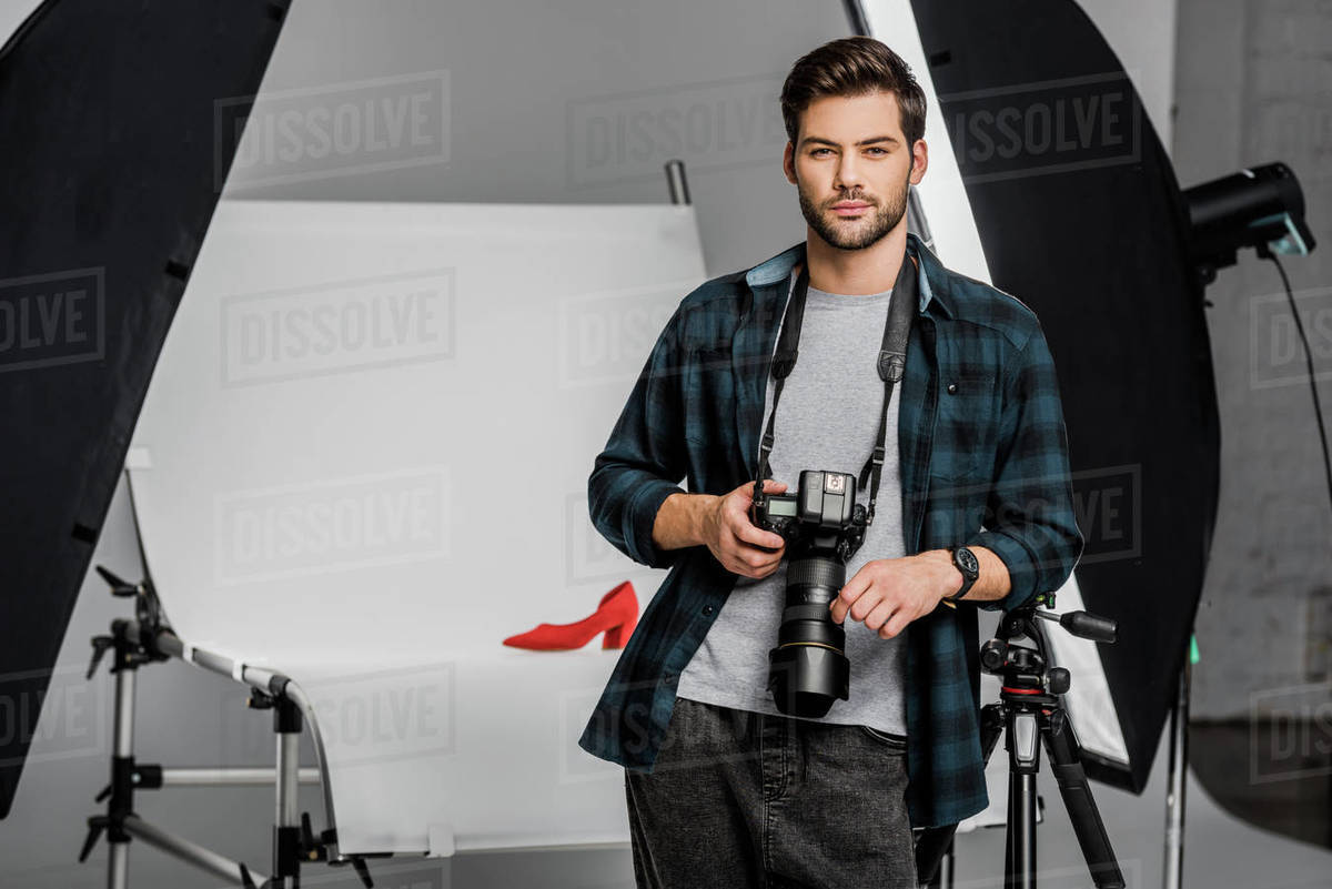 Handsome professional young photographer looking at camera in studio ...